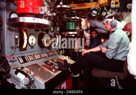 Sailors monitor the gauges on a control panel in the engine room aboard ...