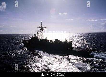 A silhouetted port view of the guided missile cruiser USS BUNKER HILL ...