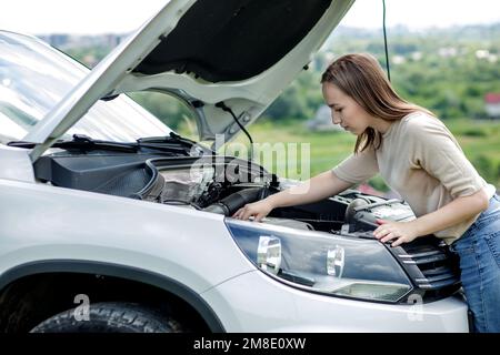 Confused female driver standing outside her car with the hood up and ...