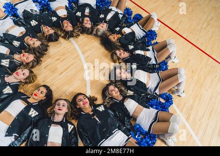 A group of cheerleaders lying on the floor forming a circle with their ...