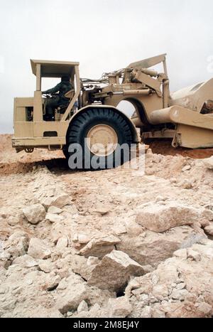A Seabee drives a motorized earthmoving scraper along a road being ...