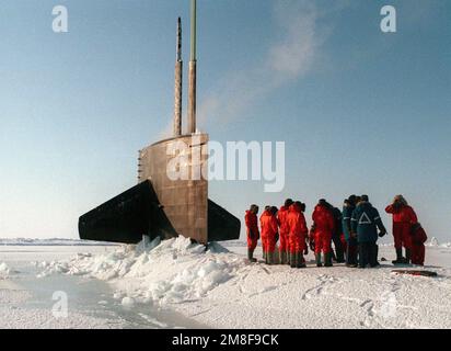 Crewmen and a group of official visitors stand on the ice a top the ...