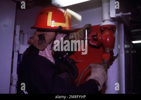 A crewman wearing oxygen breathing apparatus aims the nozzle of a water ...