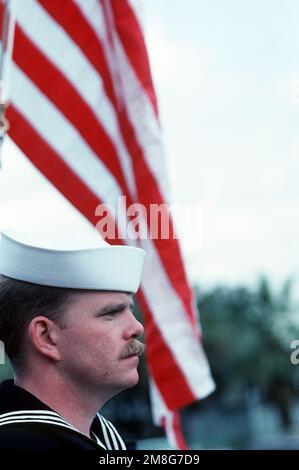 A sailor stands beside the national ensign on the stern of the frigate ...