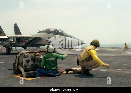 A flight deck officer and a catapult crewman stand by as an F-14A ...