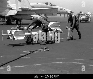 Aviation ordnancemen move a weapons skid into place in front of a ...