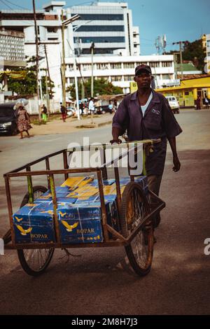 Asian worker pushing metal cart for manual labor on paved outdoor path ...