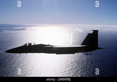 An aerial left side view of an F-15C flying between two land formations ...