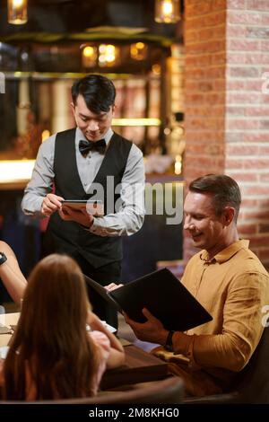 Man ordering meal at fancy restaurant table, waiter standing behind ...