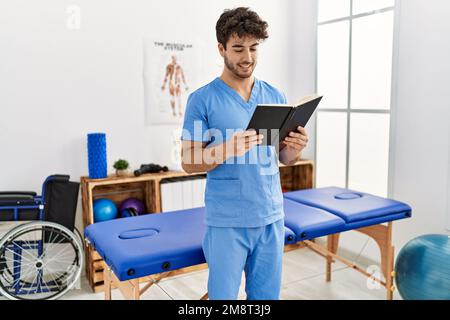 Young hispanic man wearing physio therapist uniform holding clipboard ...