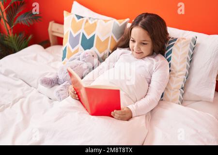 Adorable hispanic toddler reading book standing at bedroom Stock Photo ...