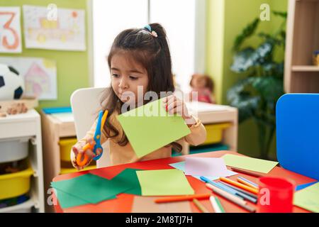 Adorable hispanic girl student sitting on table drawing on paper at ...