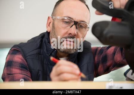 Carpenter marking pine wood plank for cutting in woodwork workshop ...