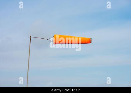 A bright orange windsock being blown horizontally in strong winds by an ...