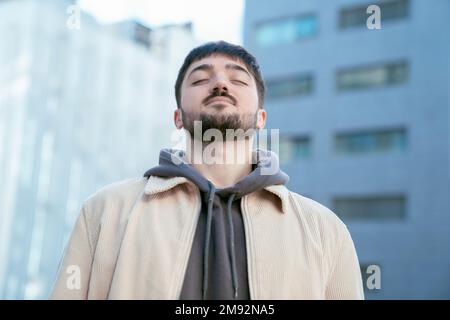 Low angle of calm thoughtful bearded guy in casual clothes standing on ...