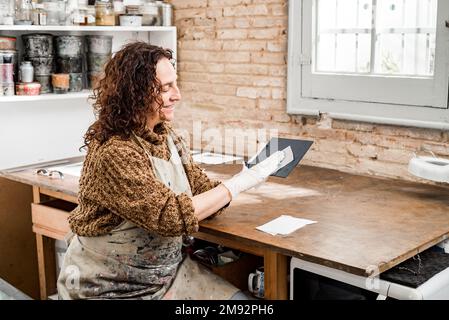 Middle aged craftswoman in dirty apron inspecting metal plate for ...