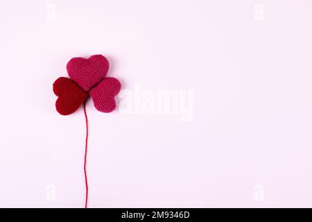 Red crocheted hearts are laid out in the shape of a balloons on a pink ...