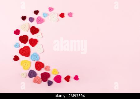 Red crocheted hearts are laid out in the shape of a flower clover on a ...