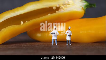Two miniature chefs standing with yellow paprika and King oyster ...