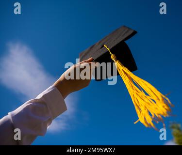 Close-up of a woman's hand with a graduation cap against the blue sky ...