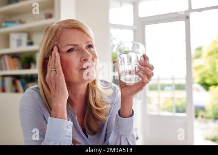 Menopause. Woman with glass of water suffering from heat flash at ...