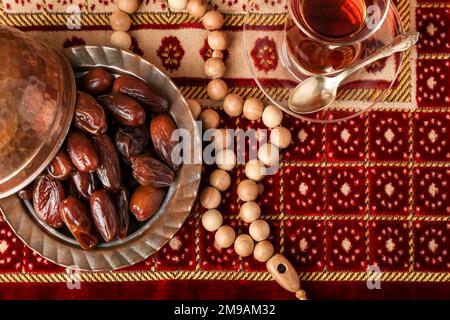 Plate with dates, prayer beads, glass of tea and teapot for Ramadan on ...