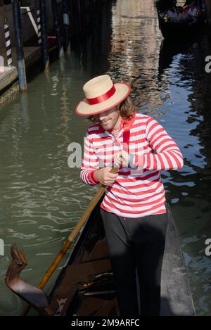 A gondolier in a traditional red and white hooped shirt sits resting in ...