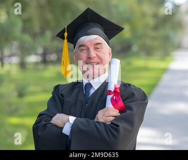 Portrait of an elderly man in a graduation gown and with a diploma in ...