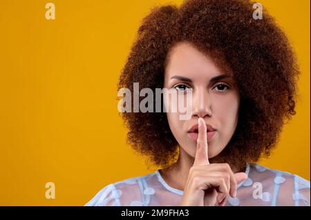 pretty woman showing hush sign and pointing with hand isolated on beige ...