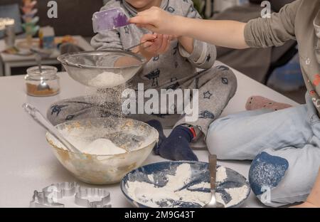 Children adding flour to a large sieve for a cake mixture Stock Photo ...