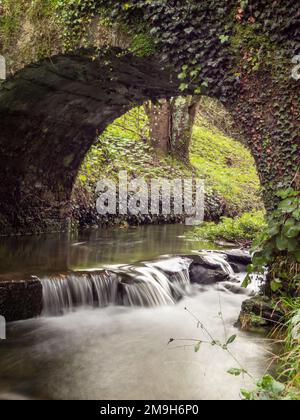 A vertical shot of foamy small waterfall under rocky mountain in ...
