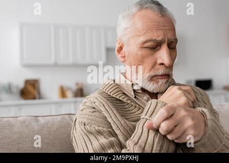 senior man with parkinson disease sitting on couch in knitted cardigan ...