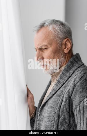 side view of aged man with alzheimer disease looking away near window ...