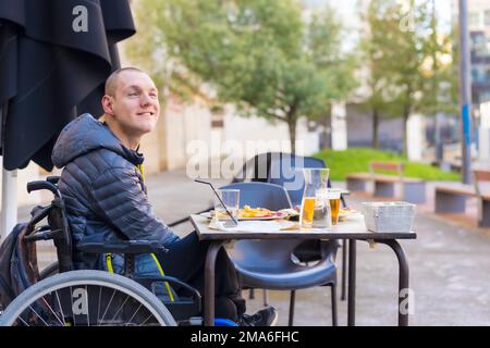 A disabled person eating on the terrace of a restaurant with a friend ...