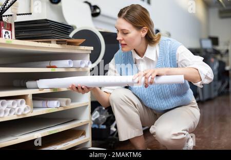 Woman employee at copy center putting roll paper on shelves Stock Photo ...