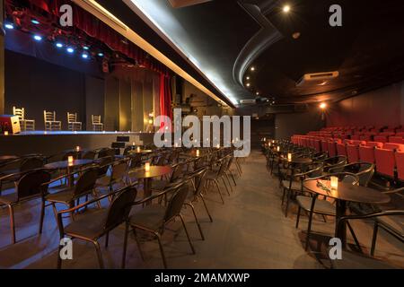 An empty theater with stalls with tables and a stage with four chairs ...