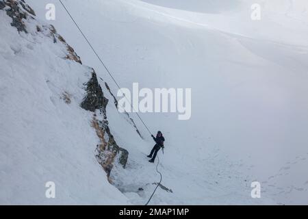 Silhouette of young man abseiling down from a snowy cliff. Climber ...