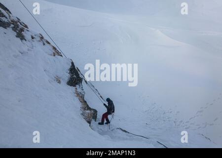 Silhouette of young man abseiling down from a snowy cliff. Climber ...