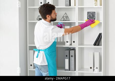 Male janitor cleaning shelving unit with rug and spray in room Stock ...