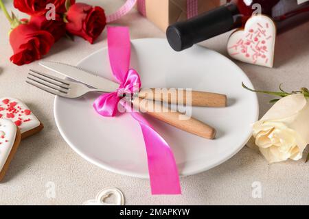 Plate and cutlery tied with pink ribbon on light table. Valentine's Day ...