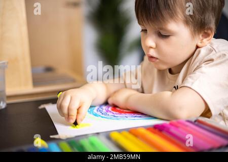 Enthusiastic male kid drawing multicolor rainbow paper sheet closeup ...