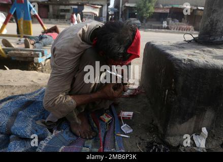 A Pakistani drug addict smokes heroin on the side of the road in ...