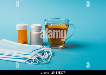 Medical masks near pills and cup of tea with lemon on blue background ...