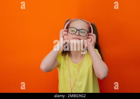 Girl with Down syndrome listens to music. Orange background. Banner Stock Photo - Alamy