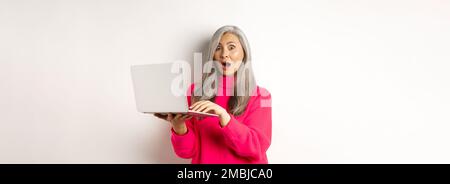 Surprised and impressed asian grandmother staring shocked at camera ...