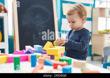 Adorable blond toddler playing with geometry blocks sitting on floor at ...