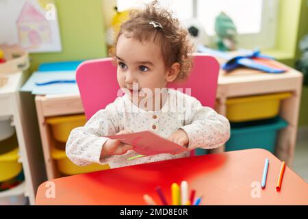Adorable hispanic toddler student smiling confident sitting on table at ...