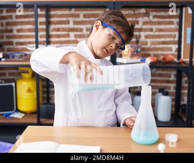Adorable hispanic boy student pouring liquid on test tube at laboratory ...