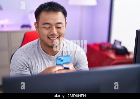 Young chinese man streamer using computer and smartphone at gaming room ...