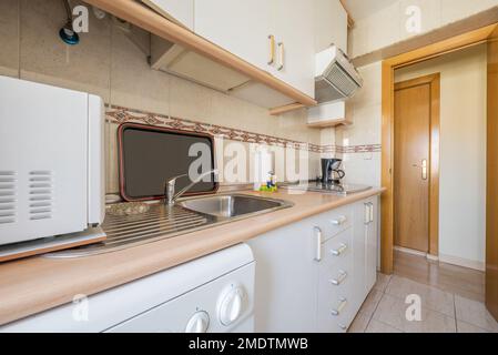 Elongated kitchen with wooden furniture, white countertop and window ...